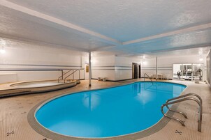 Piscina interior com chão em mosaico, escada e um banco.