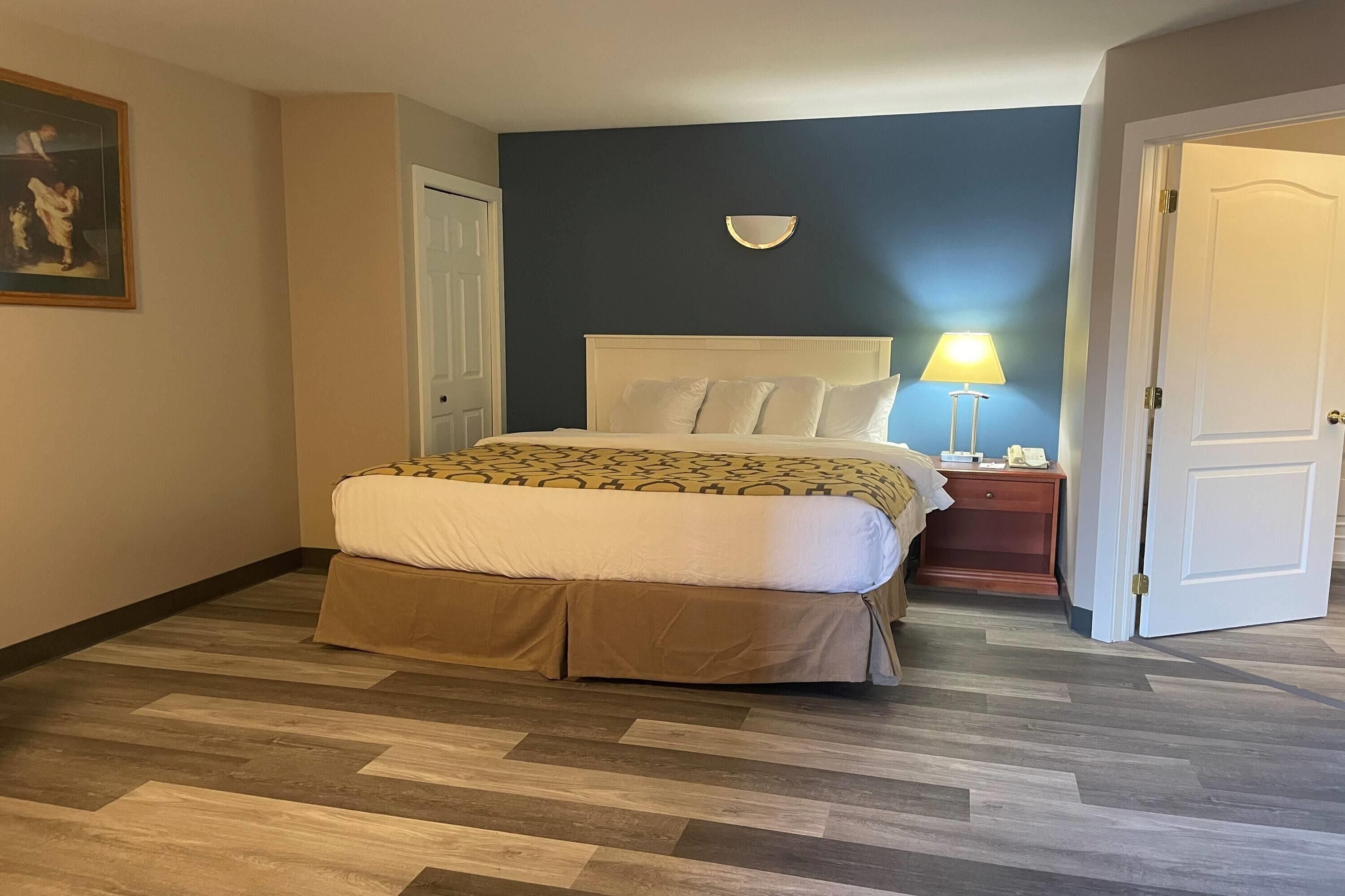Quarto de hotel com cama, mesa de cabeceira, abajur e um quadro na parede.