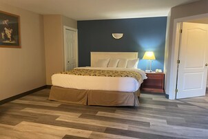 Quarto de hotel com cama, mesa de cabeceira, abajur e um quadro na parede.