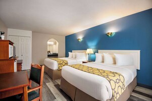 Quarto de hotel com duas camas, uma mesa de jantar e uma televisão.
