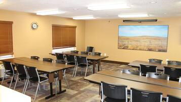 Uma sala de conferência com mesas e cadeiras, um relógio na parede e uma janela grande com persianas.
