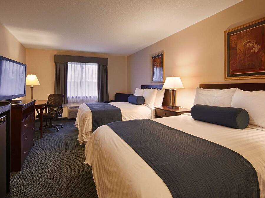 Quarto de hotel com duas camas, uma mesa de trabalho, televisão e um quadro na parede.