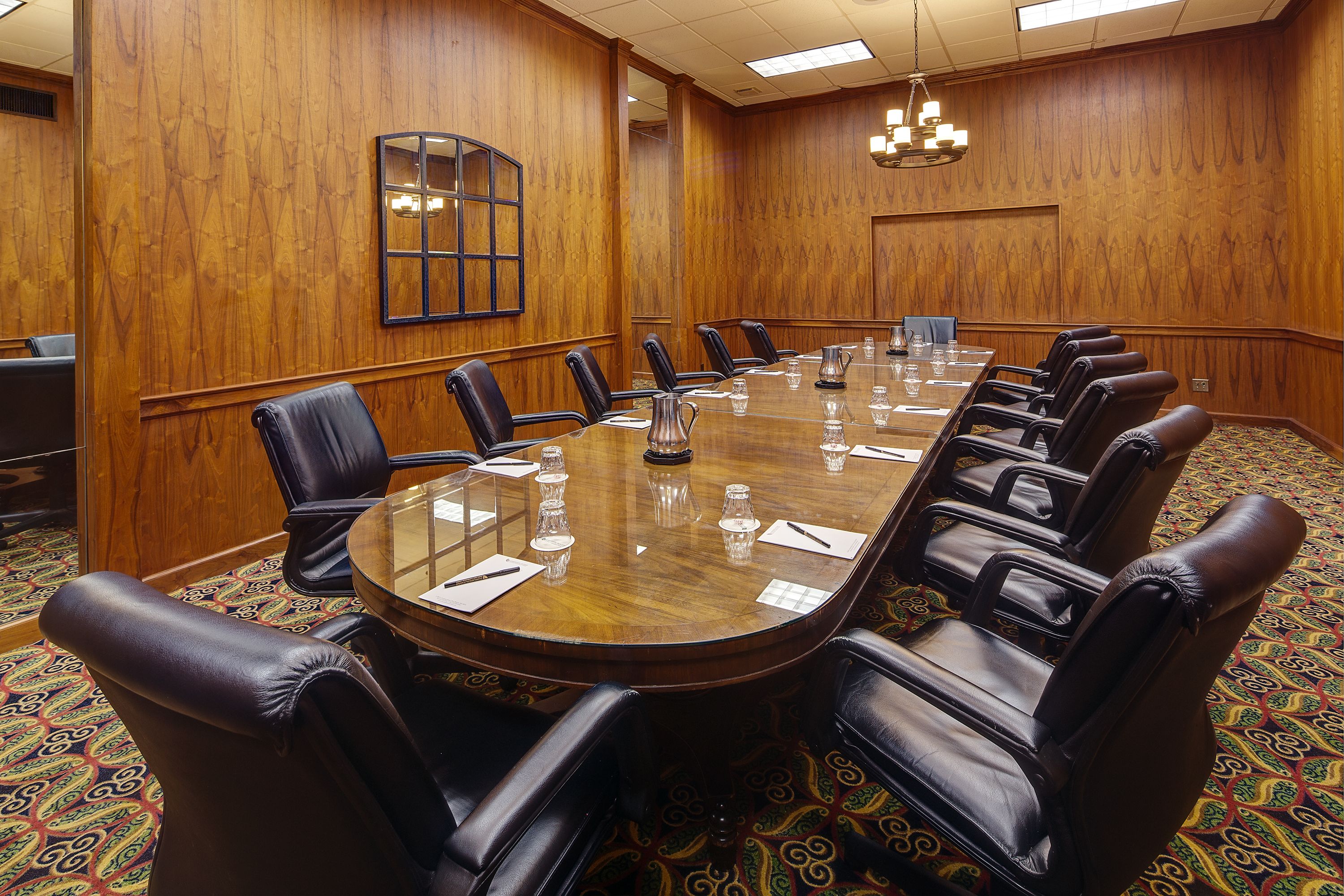 Uma sala de conferências com parede revestida de madeira, uma grande mesa oval e cadeiras de couro.