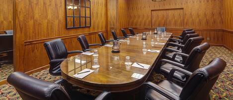 Uma sala de conferências com parede revestida de madeira, uma grande mesa oval e cadeiras de couro.