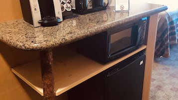 Uma cozinha compacta com cafeteira, micro-ondas e pequeno frigorífico.