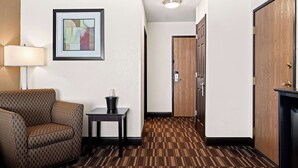 Um hall de hotel com um sofá estampado, uma mesinha com abajur e uma obra de arte emoldurada na parede.