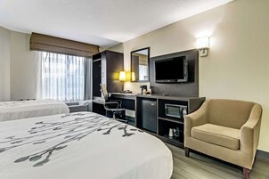 Quarto de hotel com duas camas, uma escrivaninha com cadeira, televisão e sofá.