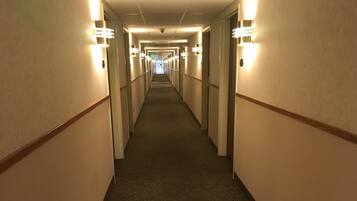 Um corredor de hotel comprido e estreito, com piso revestido de carpete e paredes, com portas alinhadas em ambos os lados.