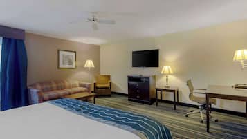 Quarto de hotel com uma cama grande, um sofá, uma escrivaninha, uma cadeira, uma televisão e duas luminárias.