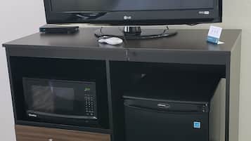 Televisão de tela plana em um móvel preto com micro-ondas e mini-geladeira.