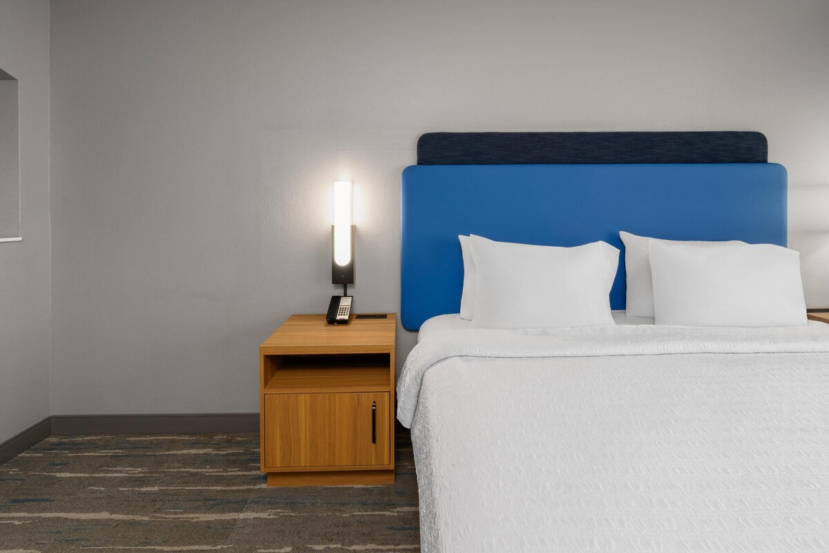 Quarto de hotel com cama, mesa de cabeceira, abajur e telefone.