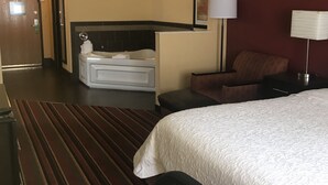 Quarto de hotel com cama, escrivaninha, cadeira, sofá, mesa de cabeceira, abajur, banheiro com banheira e porta.