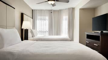 Quarto de hotel com duas camas, um ventilador de teto, uma televisão e uma mesa de cabeceira com abajur.