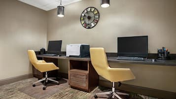 Sala de conferências com duas mesas, cadeiras, um relógio e luminárias no teto.