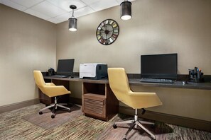 Sala de conferências com duas mesas, cadeiras, um relógio e luminárias no teto.