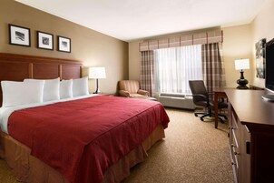 Quarto de hotel com uma cama grande, uma escrivaninha, uma cadeira, uma televisão e uma janela com cortinas.