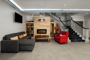 Uma sala de estar moderna com um sofá seccional cinza, uma poltrona vermelha, um painel de entretenimento de madeira e uma escada com corrimãos pretos.