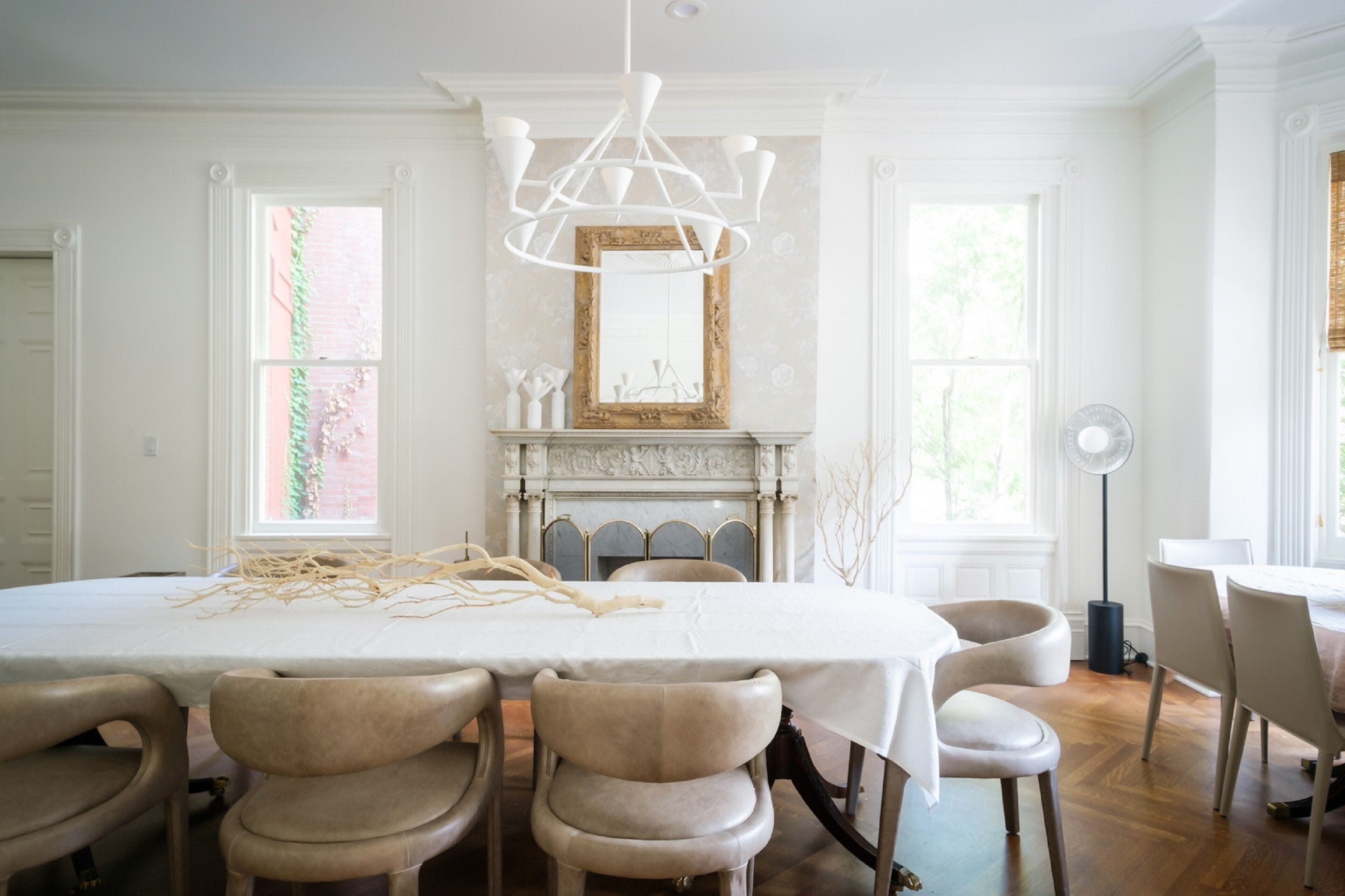 Uma sala de jantar com uma mesa grande, cadeiras, um candelabro, uma lareira e um espelho na parede.