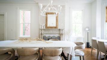 Uma sala de jantar com uma mesa grande, cadeiras, um candelabro, uma lareira e um espelho na parede.
