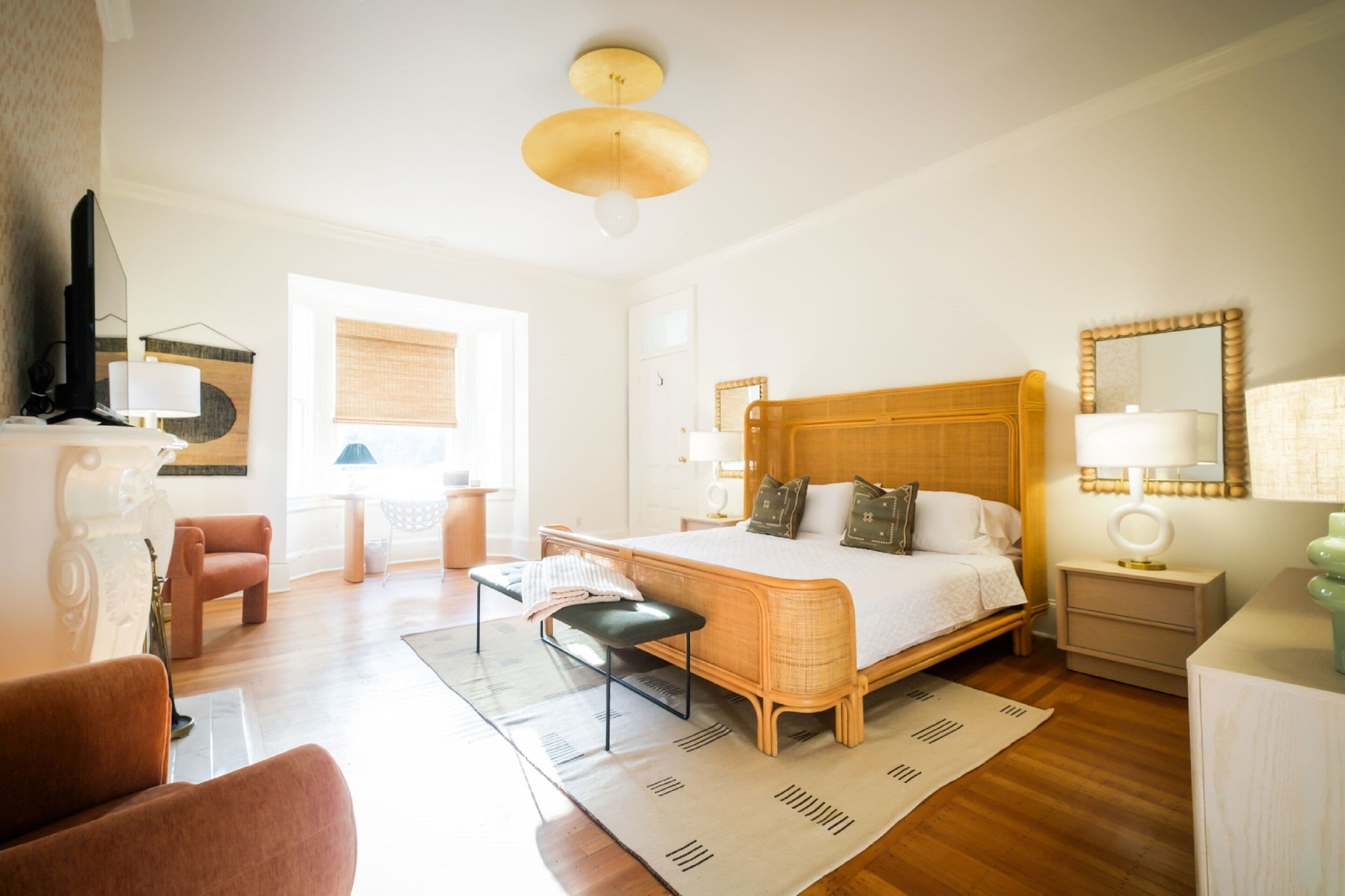 Um quarto espaçoso com uma cama grande, mesas de cabeceira, um banco e uma televisão.