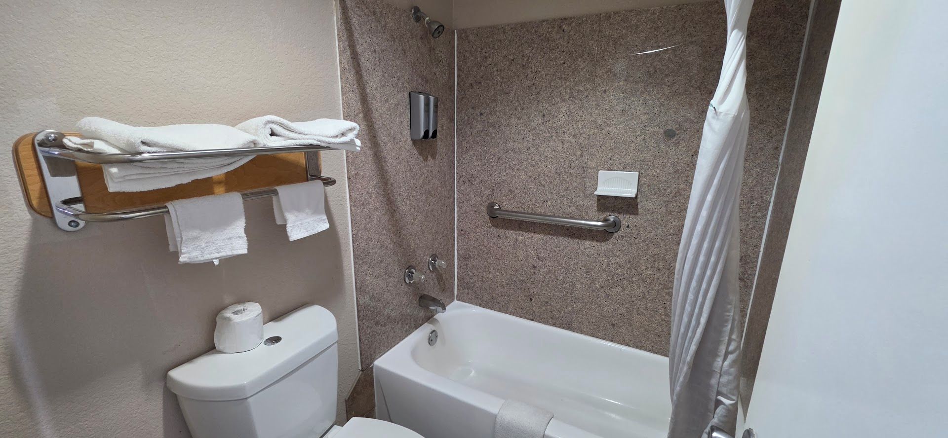 Casa de banho com sanita, banheira, porta-toalhas com toalhas e cortina de chuveiro.