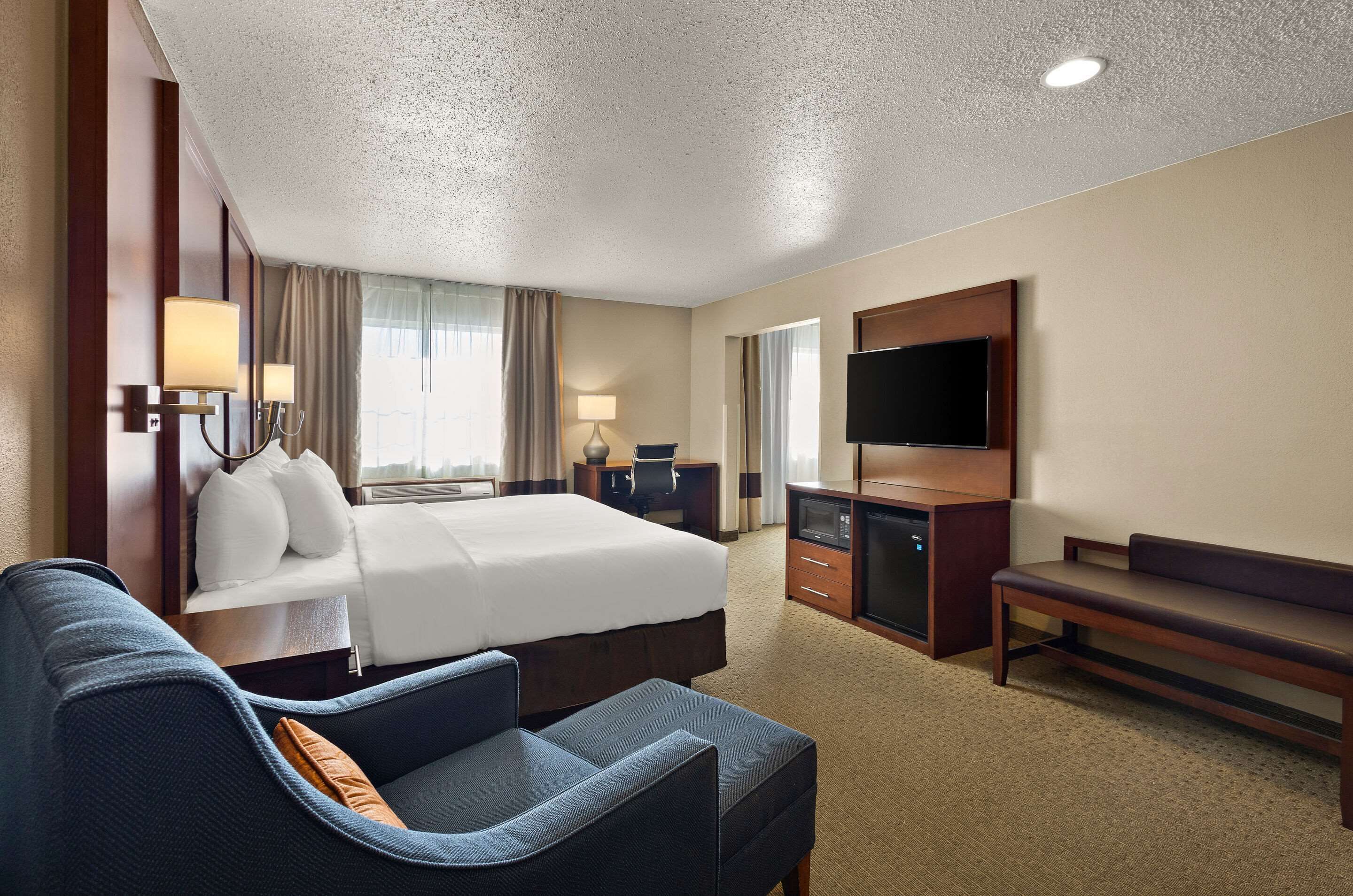 Quarto de hotel com uma cama grande, uma escrivaninha, uma cadeira, uma televisão e um banco.