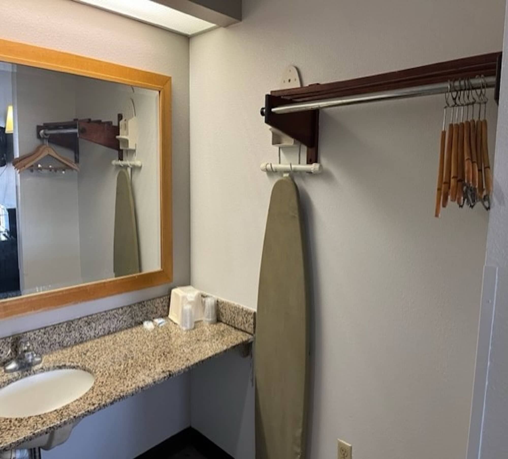 Casa de banho com bancada de granito, lavatório, espelho, tábua de passar roupa e barra de toalhas com cabides.