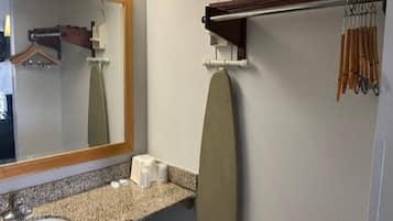 Casa de banho com bancada de granito, lavatório, espelho, tábua de passar roupa e barra de toalhas com cabides.