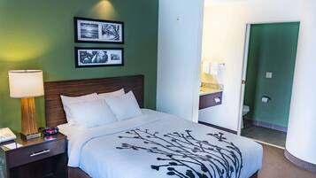 Quarto de hotel com cama, mesa de cabeceira, abajur e duas fotos emolduradas na parede.