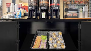 Um espaço com estação de café, duas máquinas de café, um tabuleiro de pastelaria e uma seleção de cápsulas de café.