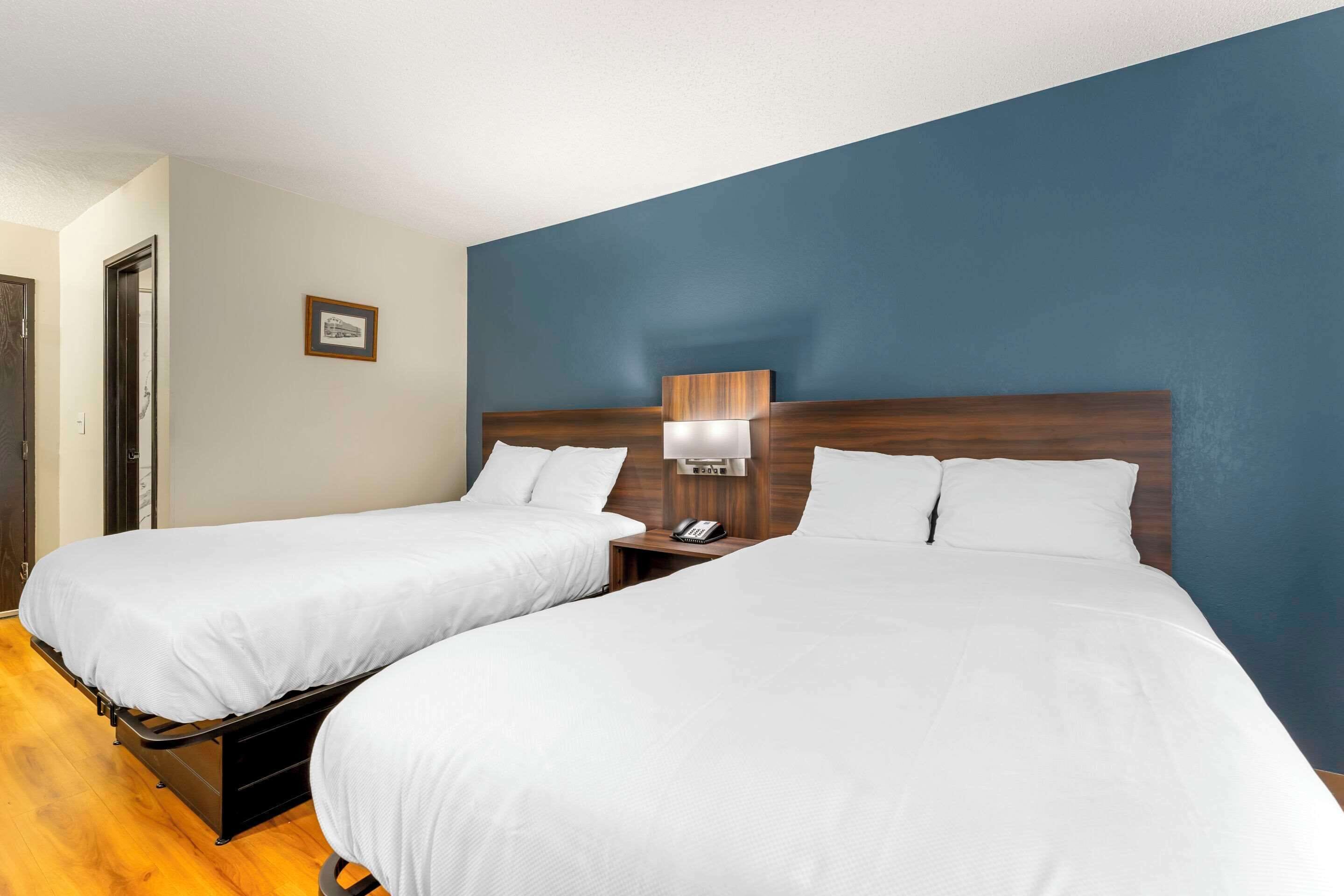 Duas camas de solteiro com cabeceiras de madeira, roupa de cama branca e mesas de cabeceira com abajures.
