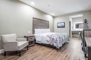 Quarto com cama, cadeira, mesa de cabeceira e espelho.