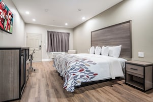 Quarto moderno com uma cama grande, mesas de cabeceira, escrivaninha e televisão na parede.