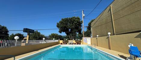 Uma piscina azul límpida com cerca branca, um letreiro da 'Quality Inn' e um muro de tijolos ao fundo.