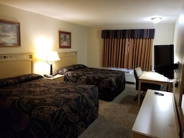 Quarto de hotel com duas camas, uma escrivaninha, uma televisão e uma luminária.