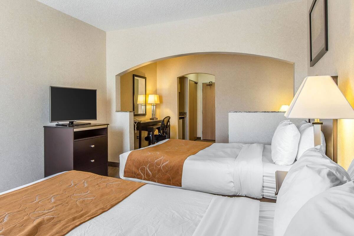 Quarto de hotel com duas camas, uma escrivaninha, uma televisão e um espelho.