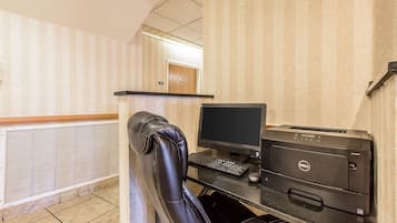 Quarto de hotel com escrivaninha, computador e impressora.