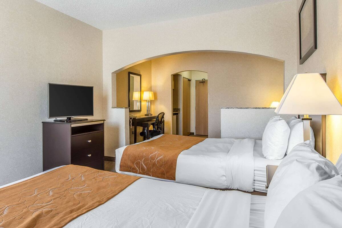 Quarto de hotel com duas camas, televisão, escrivaninha e espelho.