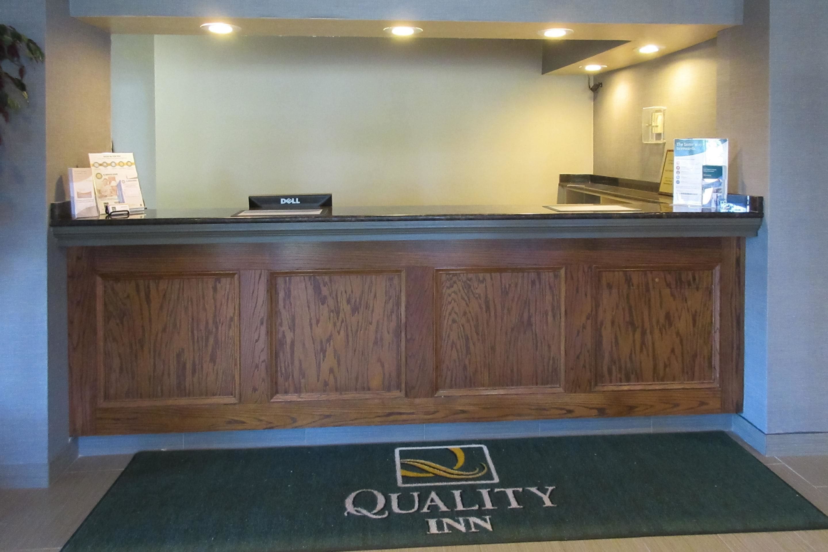 Uma mesa de recepção com design em painel de madeira, o logotipo Dell e uma placa da Quality Inn.