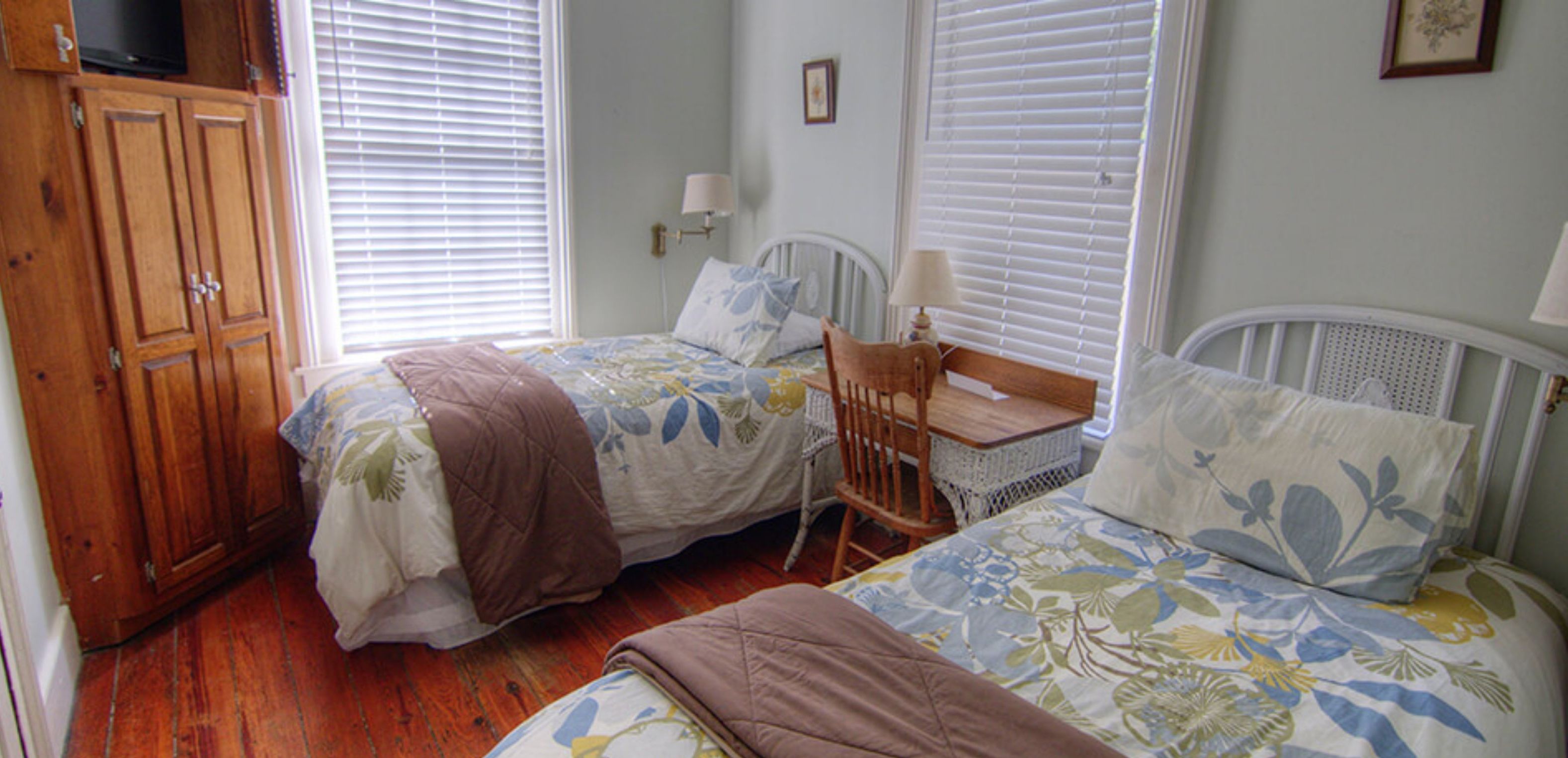 Quarto com duas camas de solteiro, móveis de madeira e uma televisão sobre um móvel.