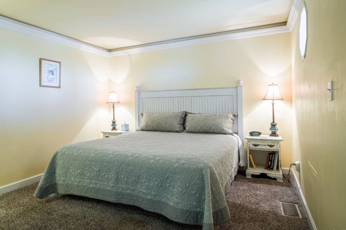 Quarto com cama, duas mesas de cabeceira, um criado-mudo e uma luminária de parede.
