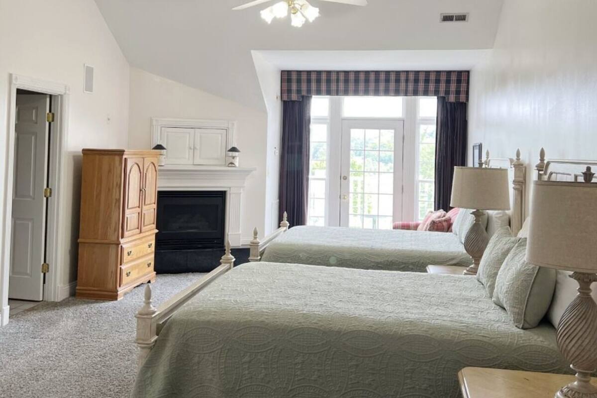 Quarto com duas camas, um armário de madeira, lareira e janela com cortinas.