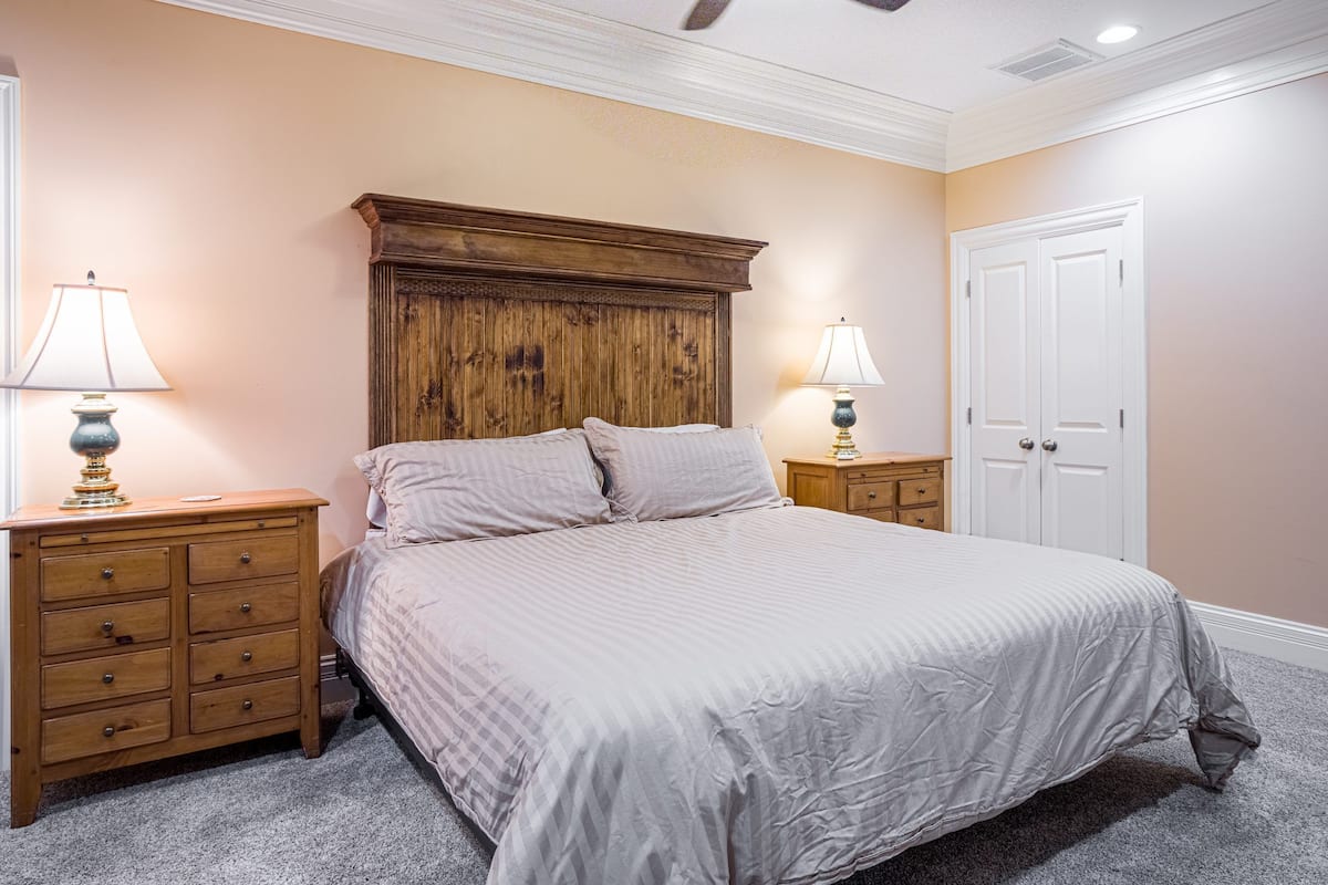 Quarto com uma cama grande, duas mesas de cabeceira, cabeceira de madeira e uma porta branca.