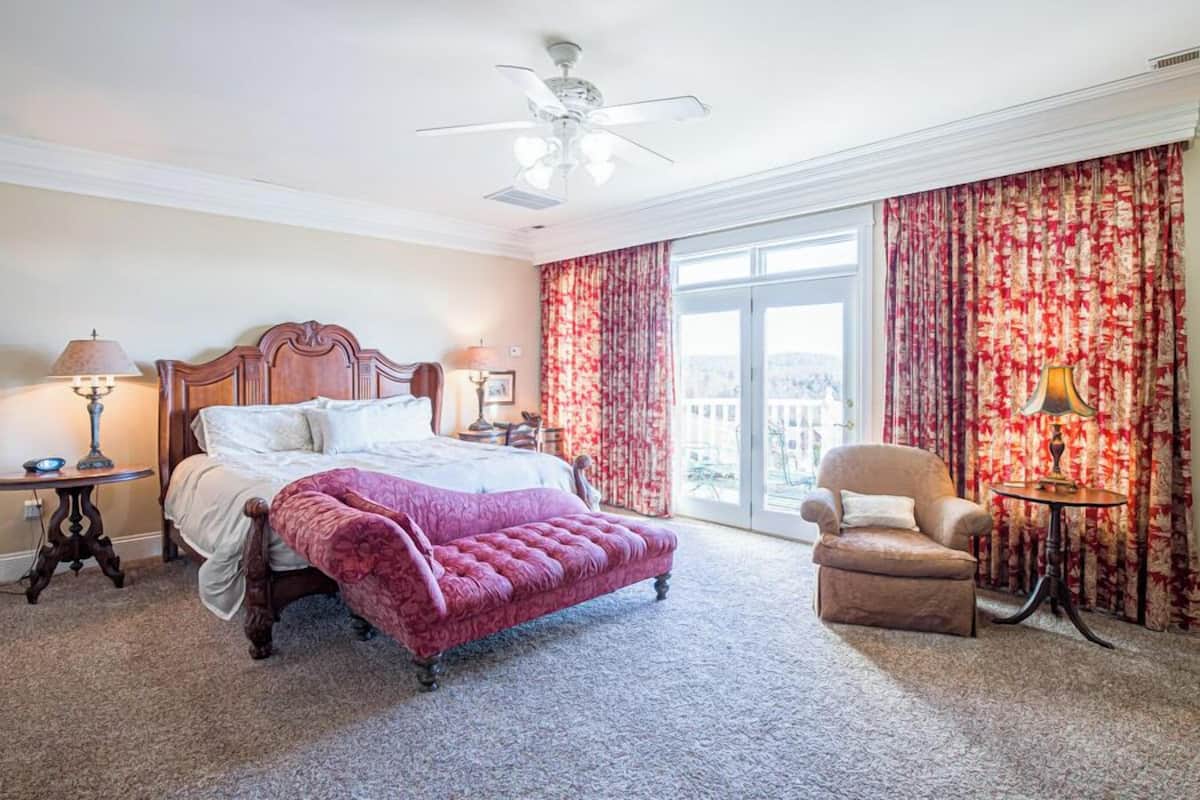 Quarto de hotel com uma cama grande, um espaço de estar com uma cadeira, uma mesa e vista pela janela.