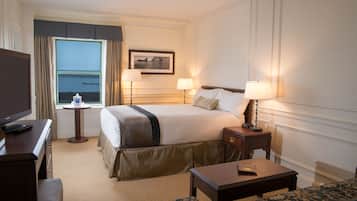 Quarto de hotel com cama, abajures, escrivaninha com televisão, mesinha e vista para o mar.