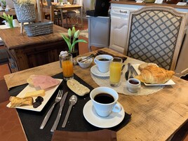 Uma mesa de café da manhã com croissants, presunto, pão, café e suco.