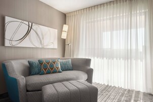 Uma sala de estar moderna com um sofá cinzento, almofadas estampadas, um abajur e um quadro abstrato grande na parede.