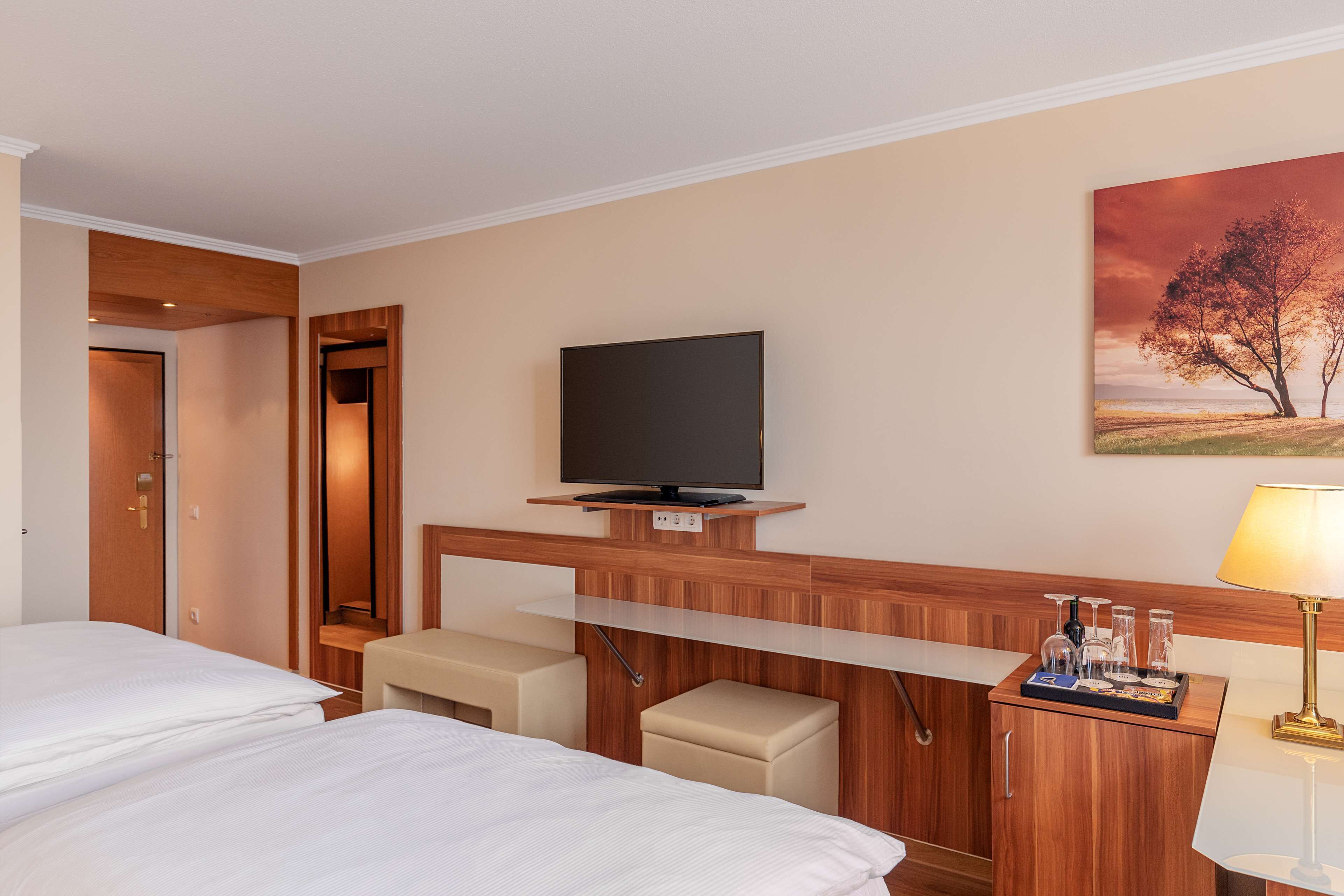 Quarto de hotel com duas camas, televisão, escrivaninha com abajur e um quadro na parede.