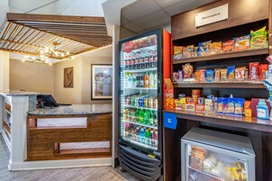 Uma área de recepção com um refrigerador Coca-Cola, prateleiras com lanches e um freezer pequeno.