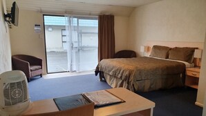 Quarto de hotel com cama, escrivaninha, cadeira, ventoinha e vista para o exterior.